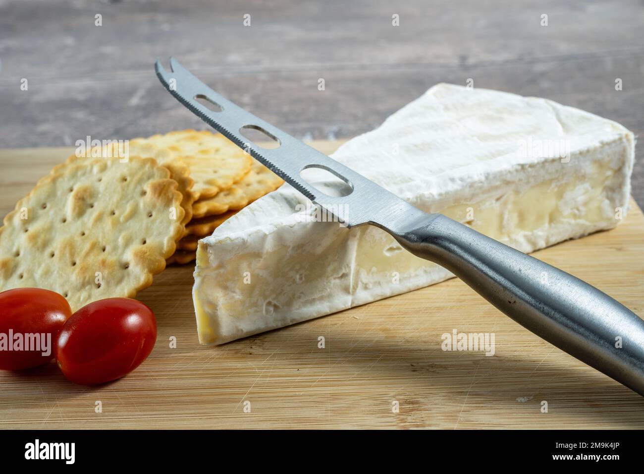 French Brie soft cheese served ed plum tomatoes and thin crackers on a ...