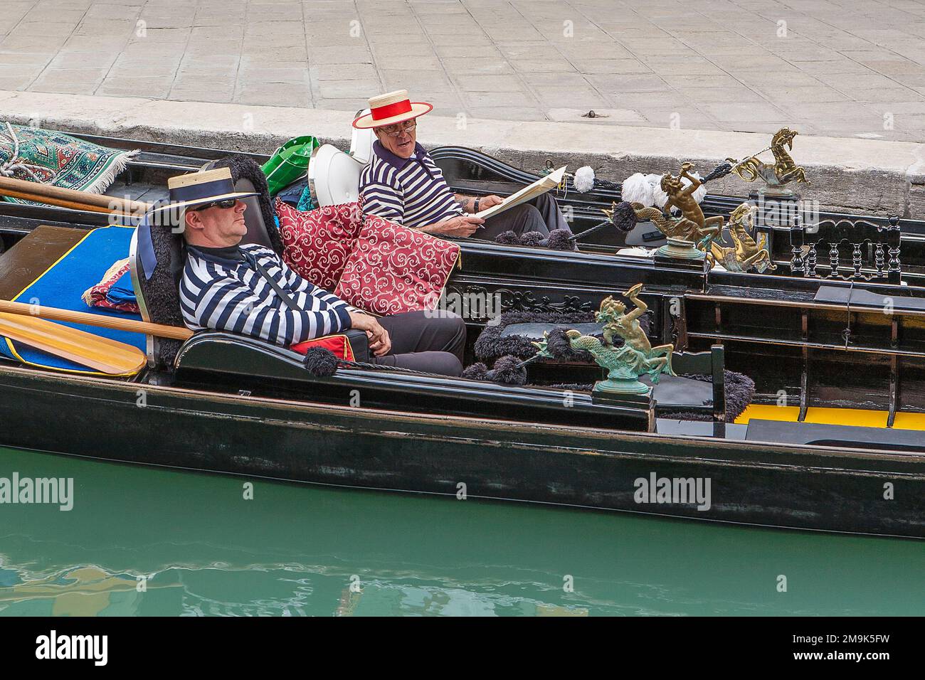 Two gondoliers resting in their gondolas parked side by side in Venice ...