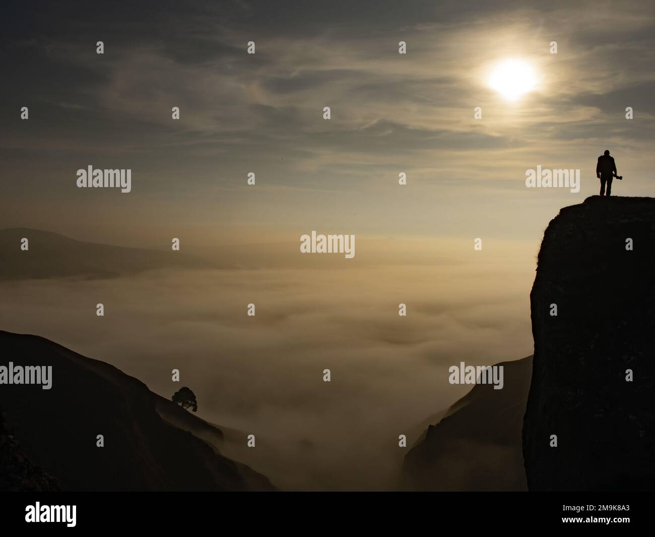 A cloud inversion peak with tree and man in silhouette during sunset ...