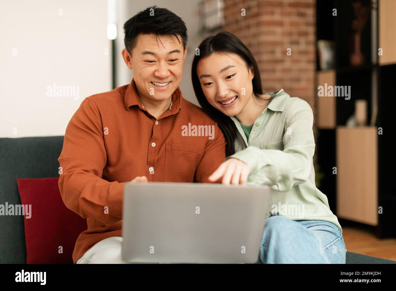 People and technology concept. Happy asian spouses using laptop at home, lady pointing at screen ...