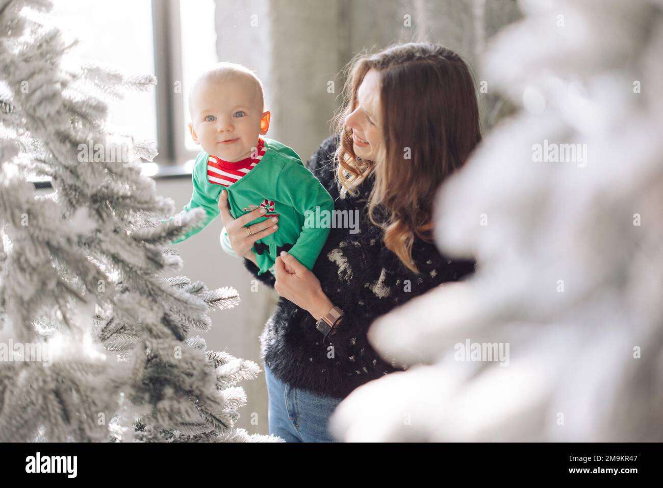 Happy mother plays with her baby son near Christmas tree decorated by ...