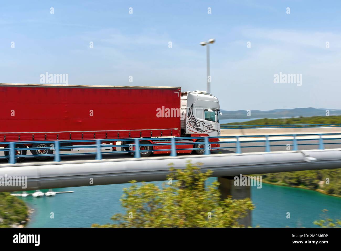 A red semi-truck driving on a motorway across the road over the sea ...