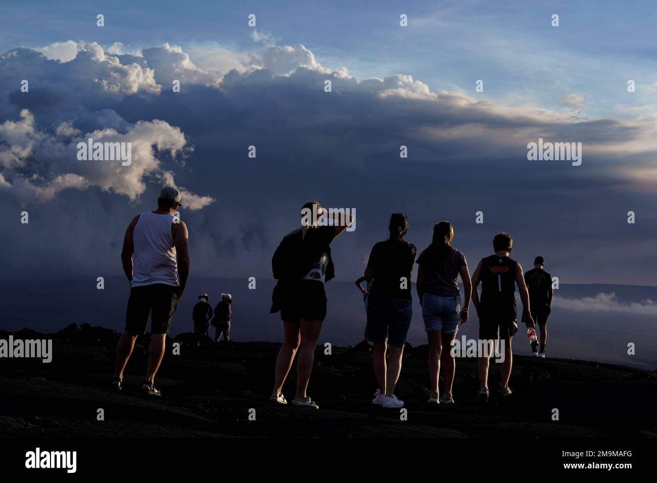 People stand on lava rock from a previous eruption near the Mauna Loa ...