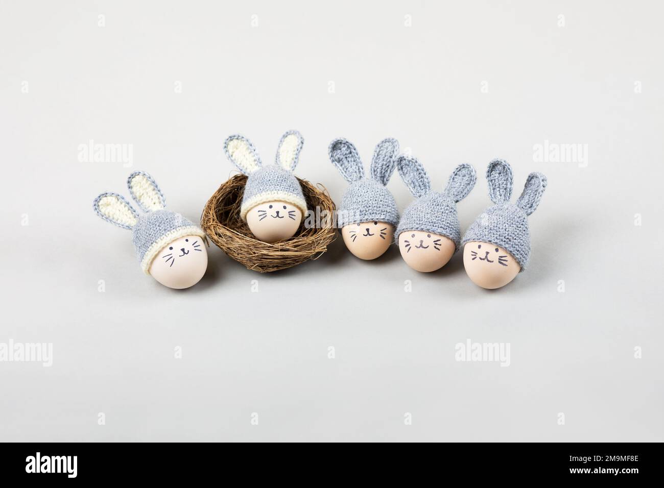 Five Easter eggs with funny faces and gray crocheted hats with bunny ...