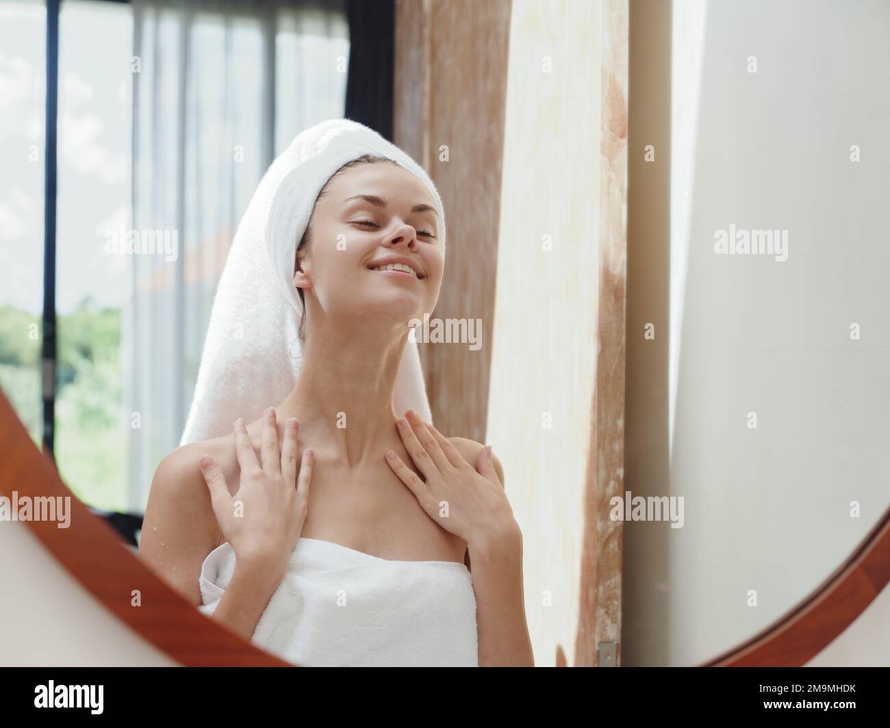 A beauty woman stands in front of a mirror after a shower in a towel on ...