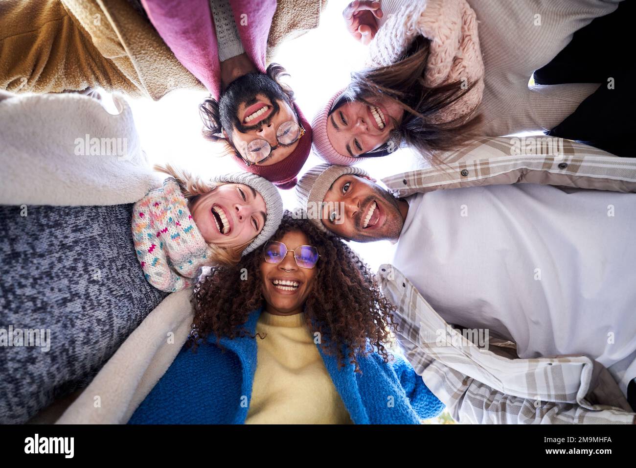 Multiracial group of happy friends doing a circle embracing, looking down to the camera ...