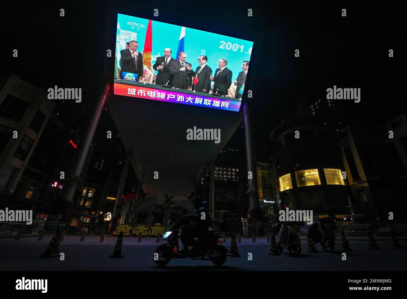 A rider passes by a large screen showing a footage of former Chinese ...