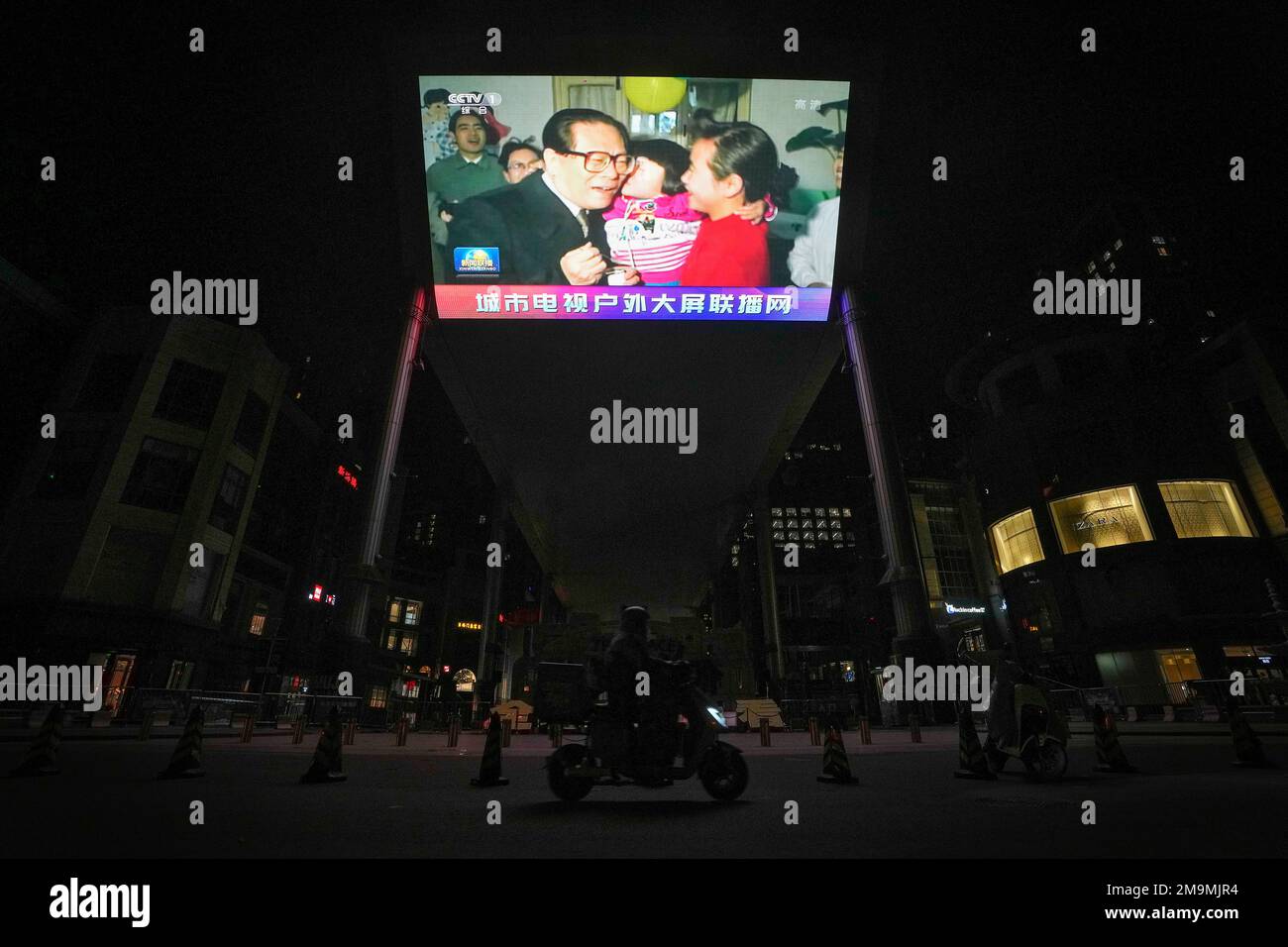 A delivery worker rides past a large screen outside a deserted shopping ...