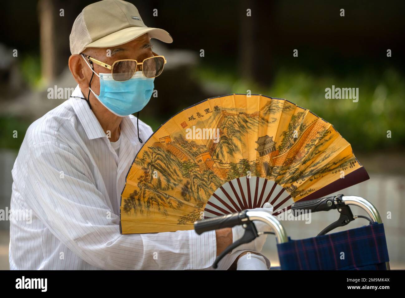 FILE - An elderly man wearing a face mask fans himself at a public park ...