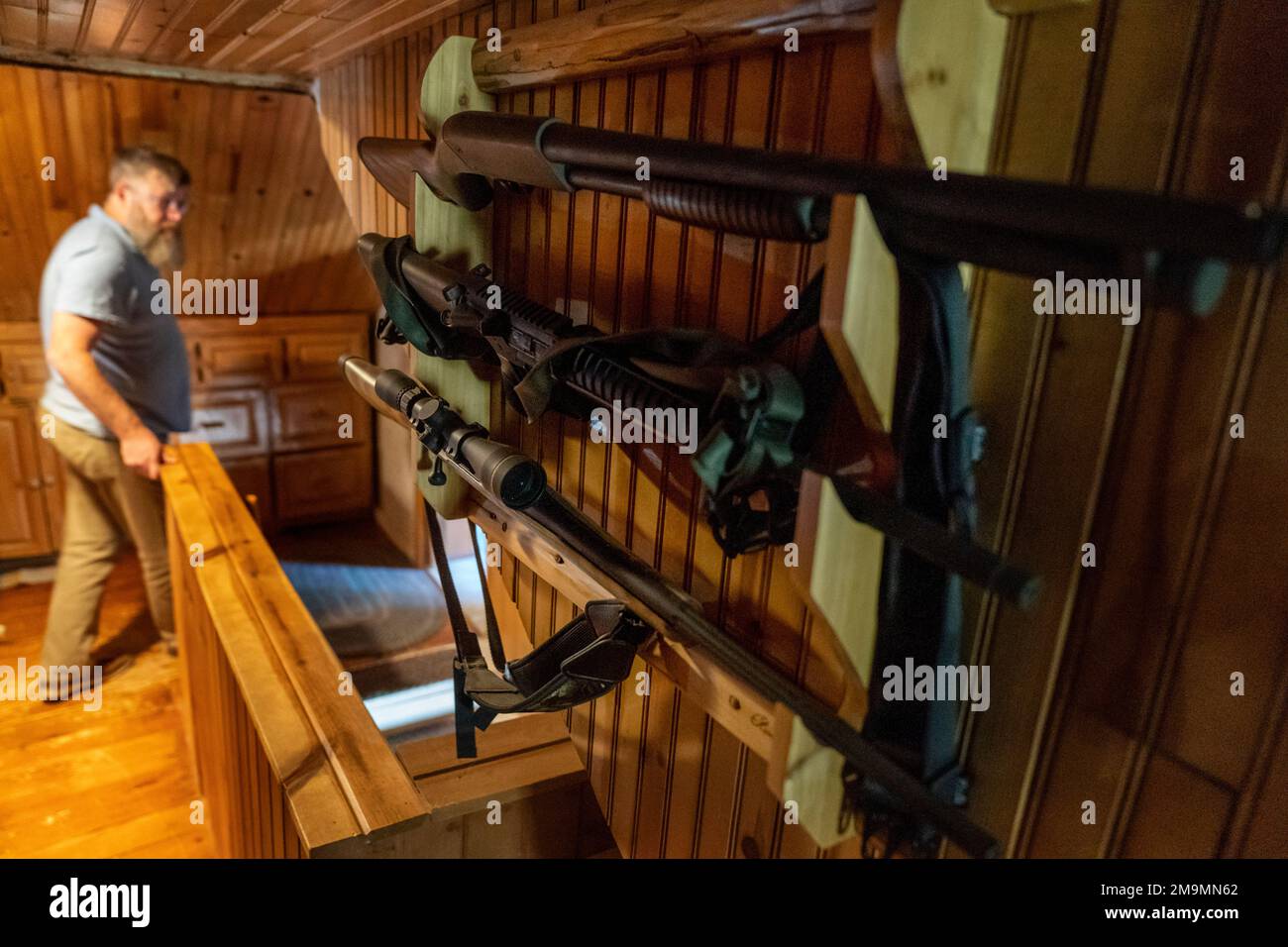 Mark Carlson walks past a gun rack holding his firearms at his home in ...