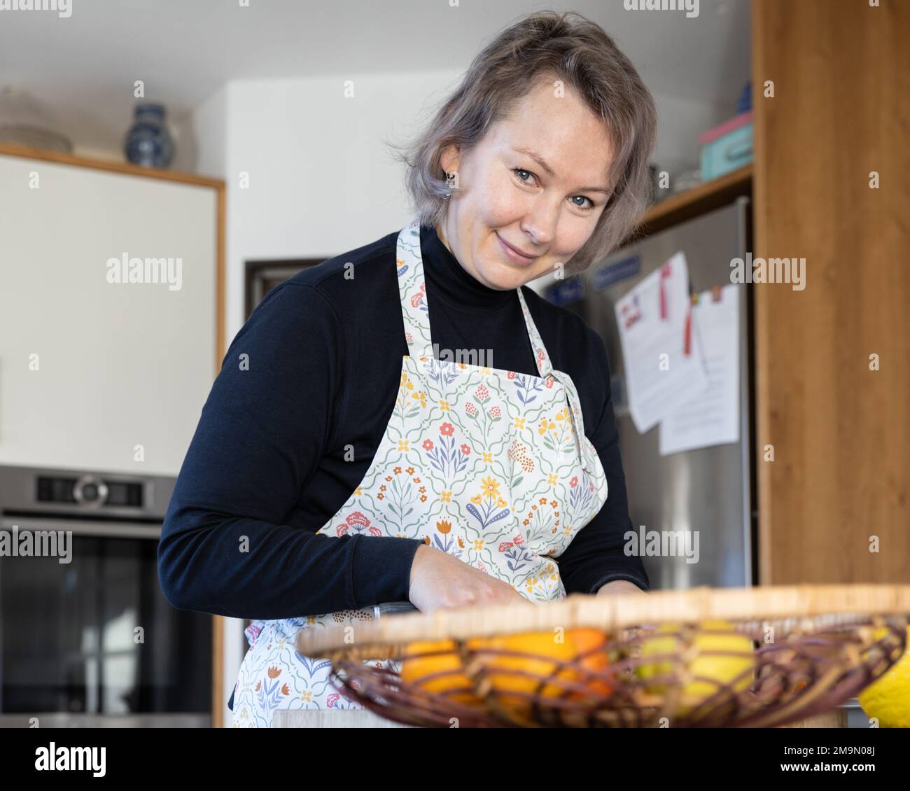 A middle-aged woman in an apron in the kitchen is engaged in cooking ...