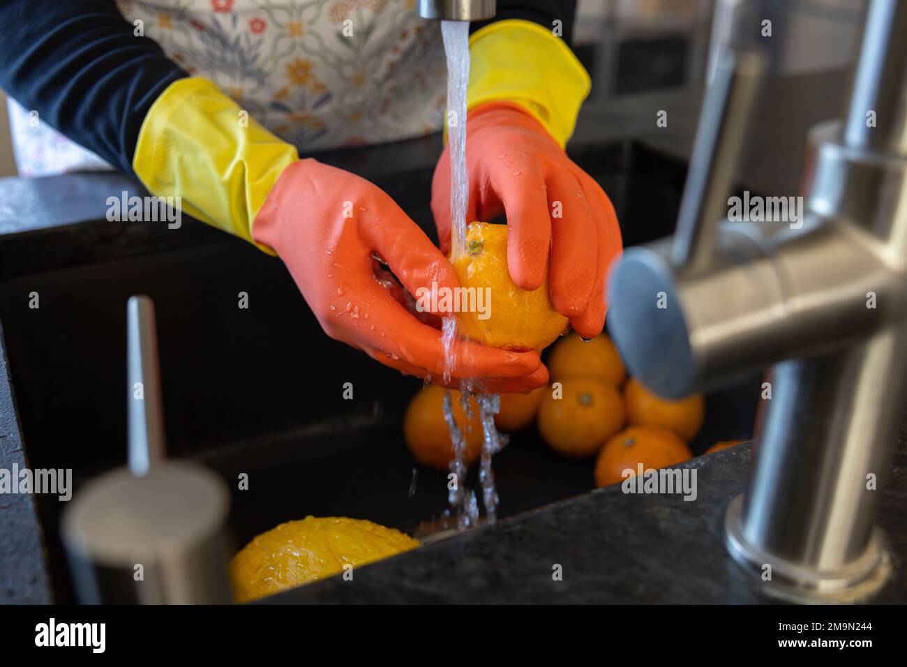 Women's hands in bright gloves wash orange fruit with tap water Stock ...