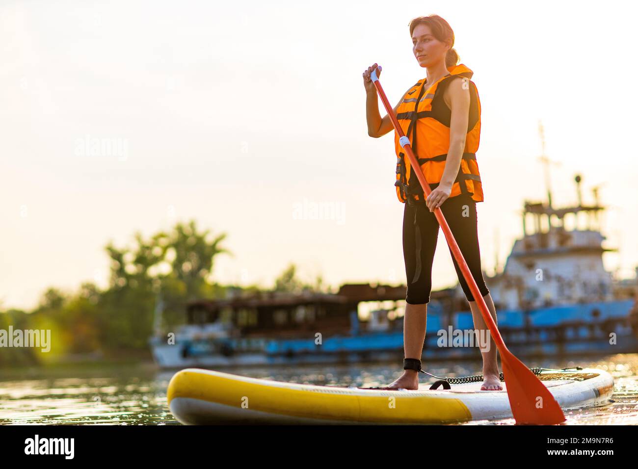 young woman in orange life jacket on supboard at river Stock Photo - Alamy