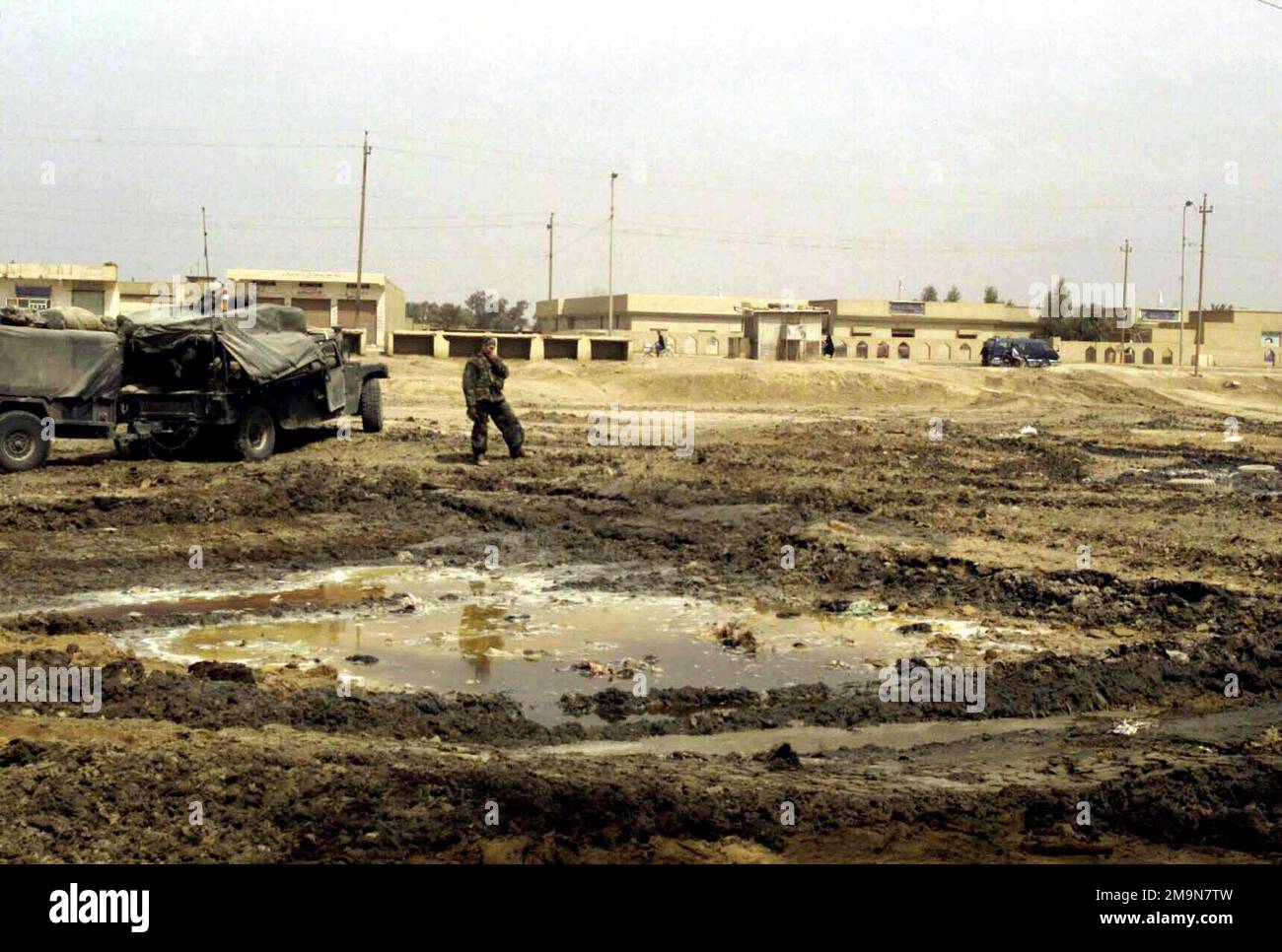In an open muddy field, US Marine Corps (USMC) personnel watch over the ...