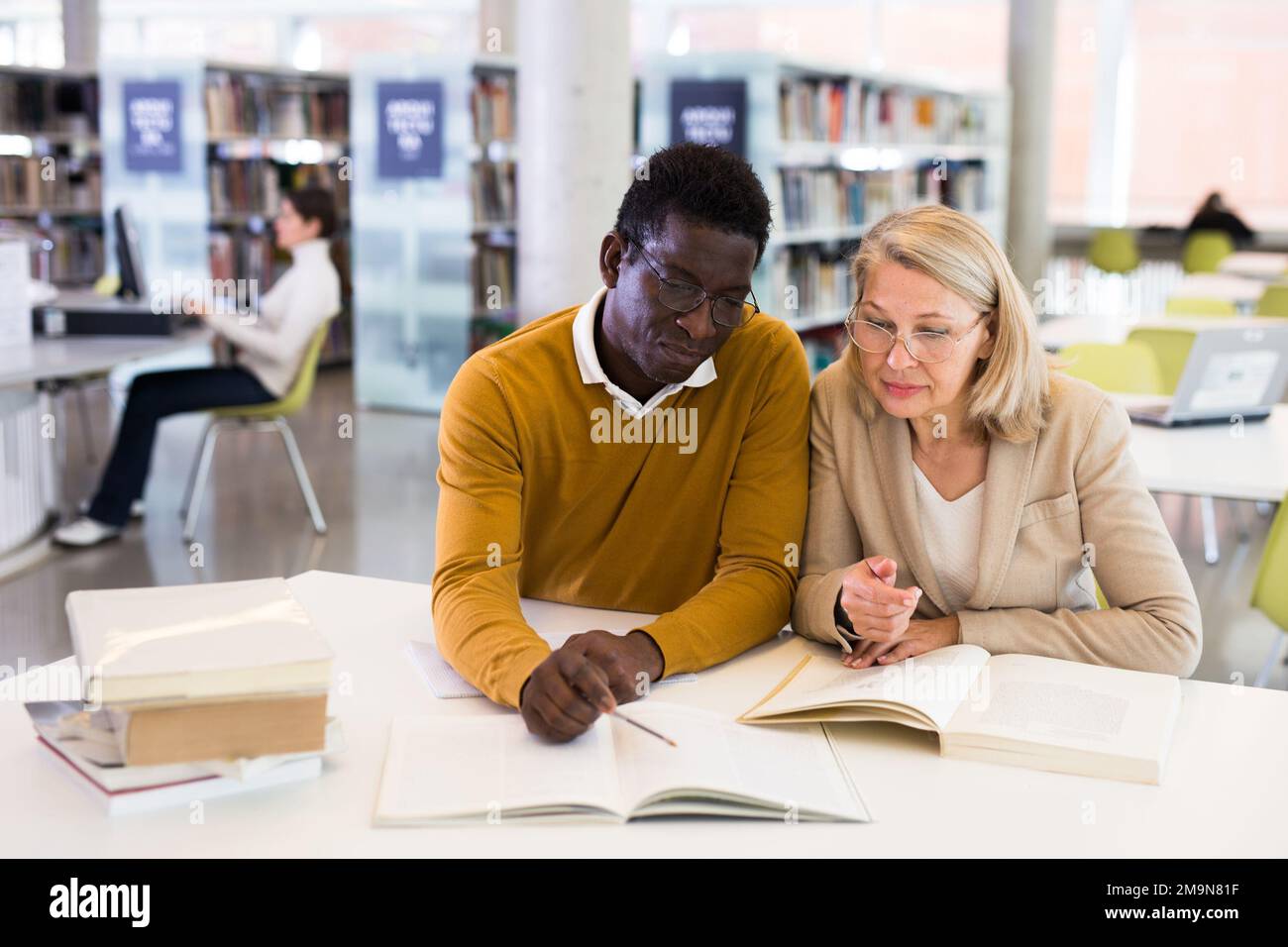 Friendly adult students preparing in library Stock Photo - Alamy