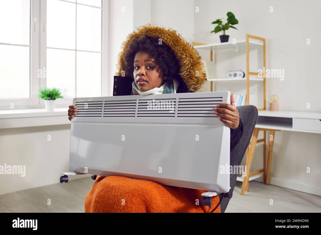 Young frozen woman sitting in a winter coat on a chair at home and ...