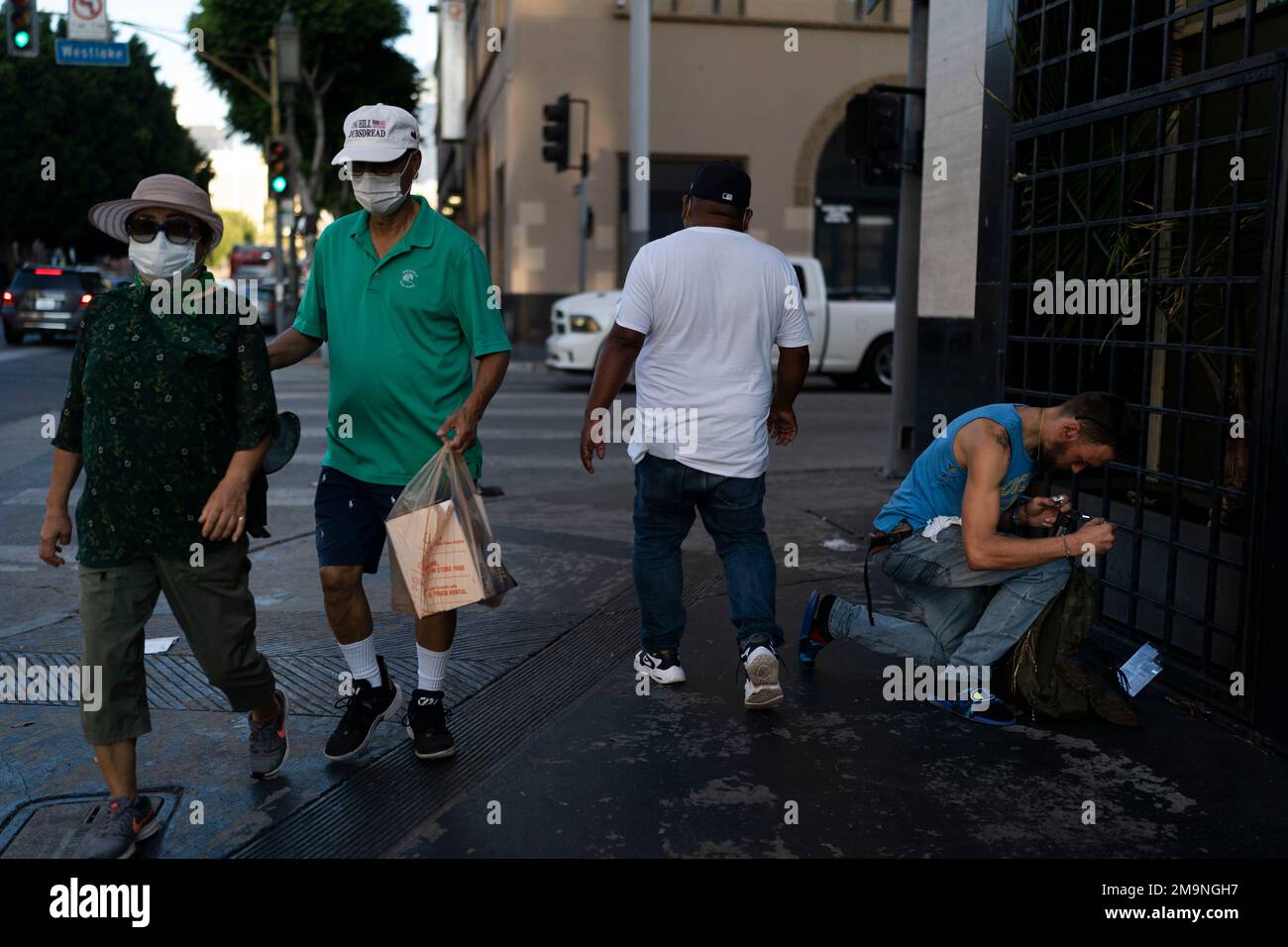 An addict kneels on a sidewalk to smoke fentanyl as pedestrians walk ...