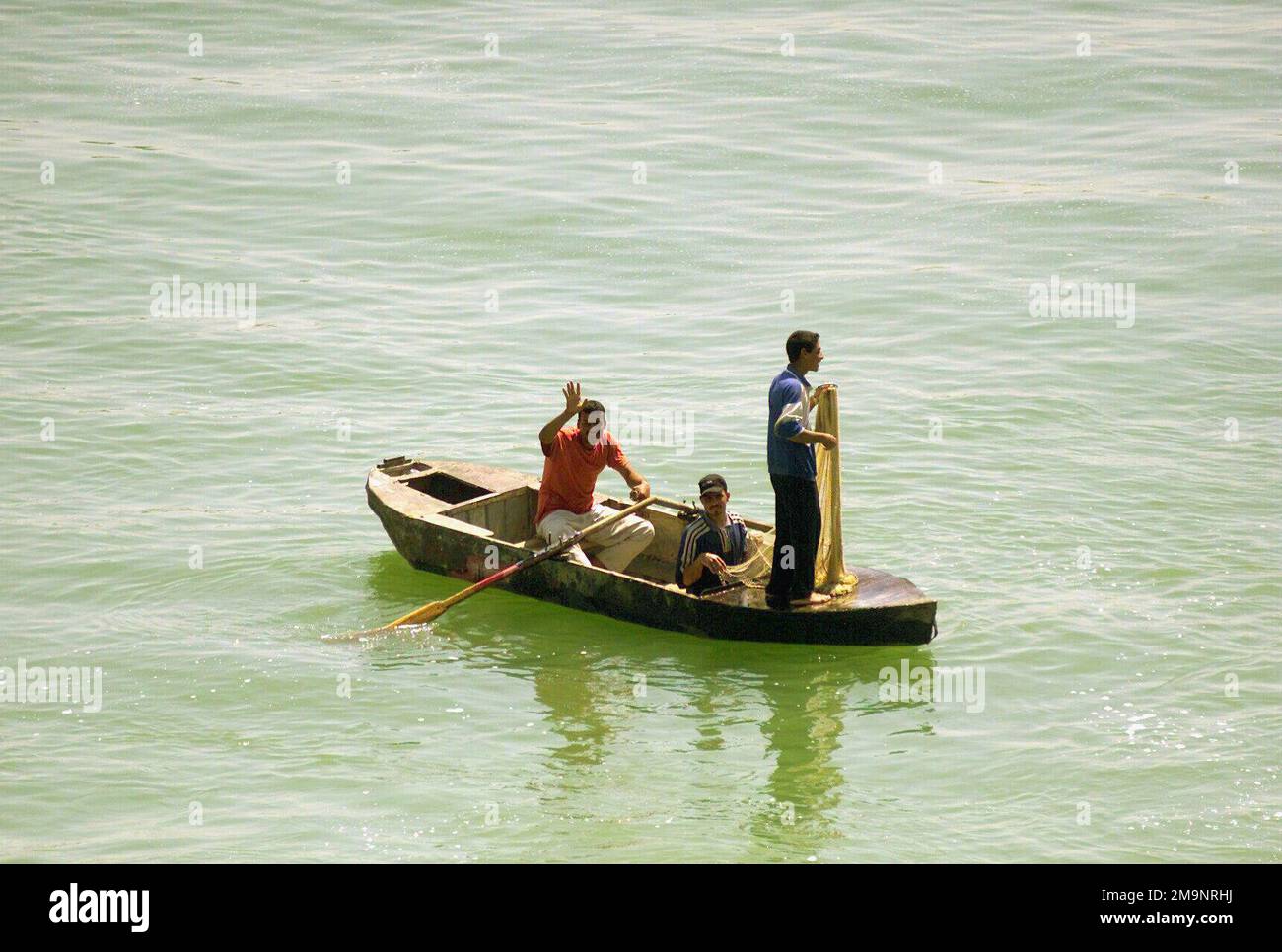 Three Iraqi fishermen wave from their boat as a US Military convoy ...