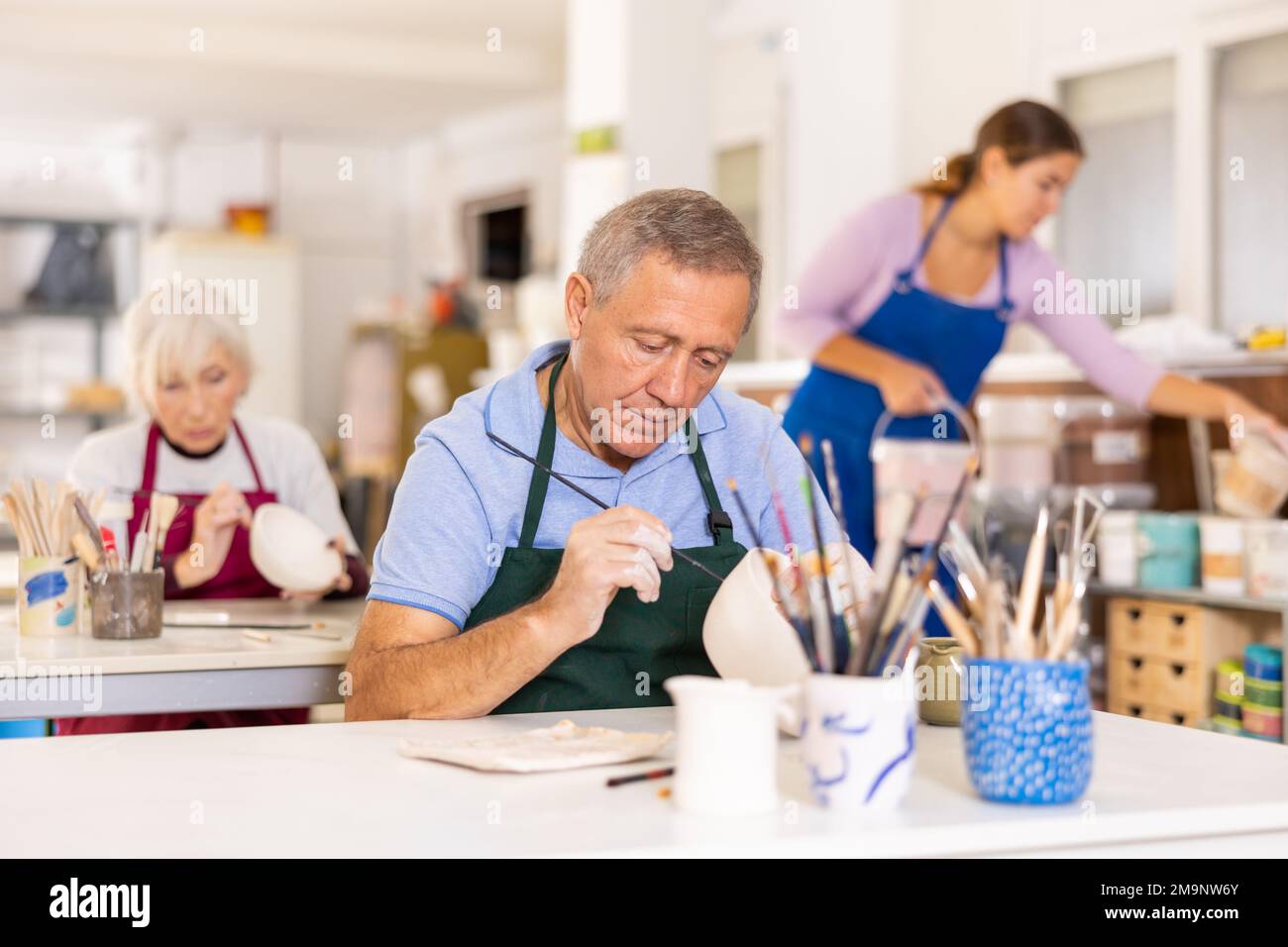 Mature craftsman painting clay plates acrylic paints in art studio ...