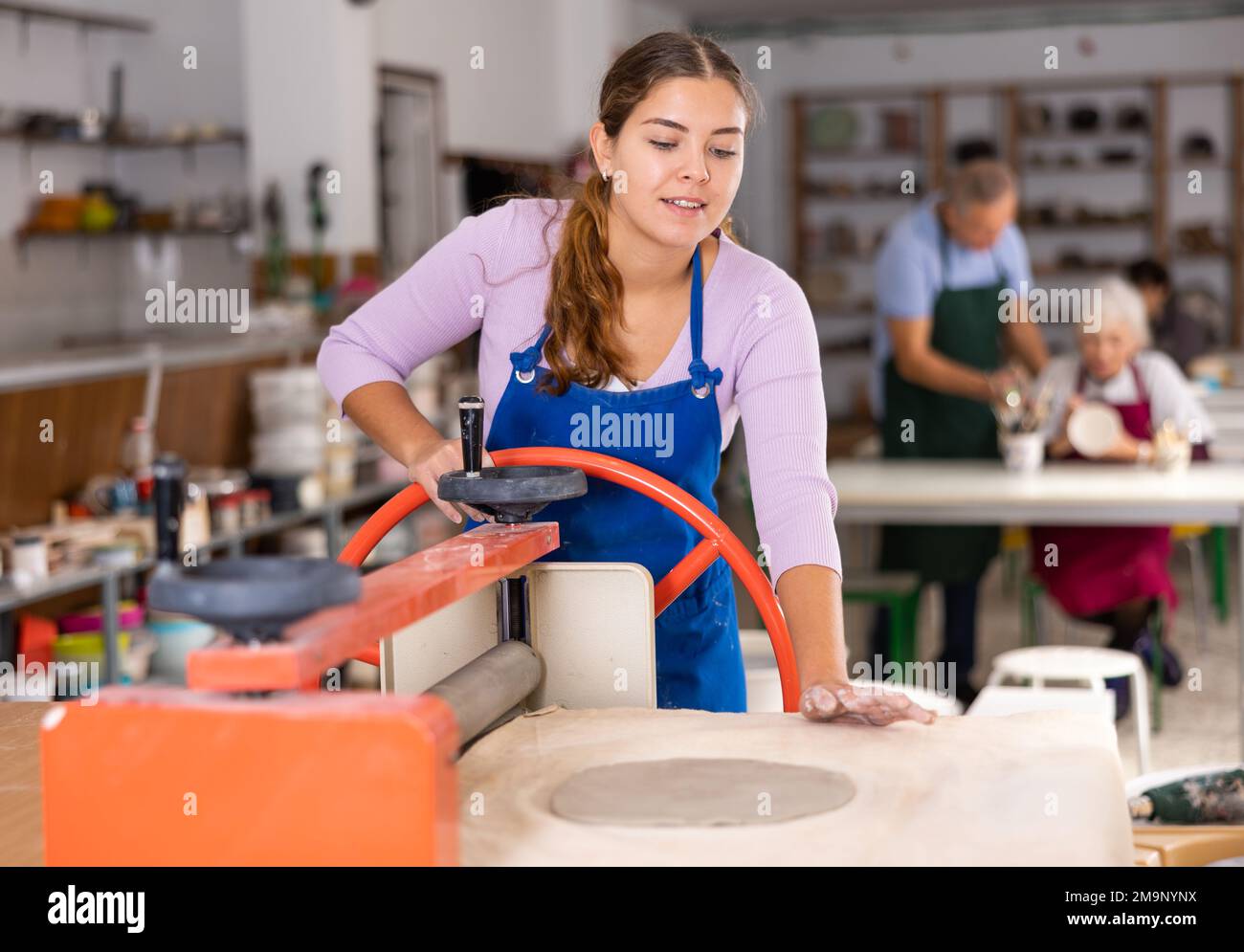 Young woman rolls out clay on craft machine clay press roller in studio ...