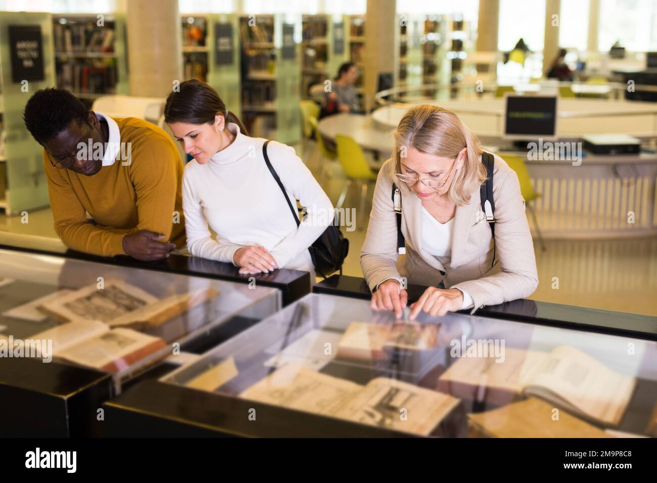 Professor and adult students read ancient books in a library showcase ...