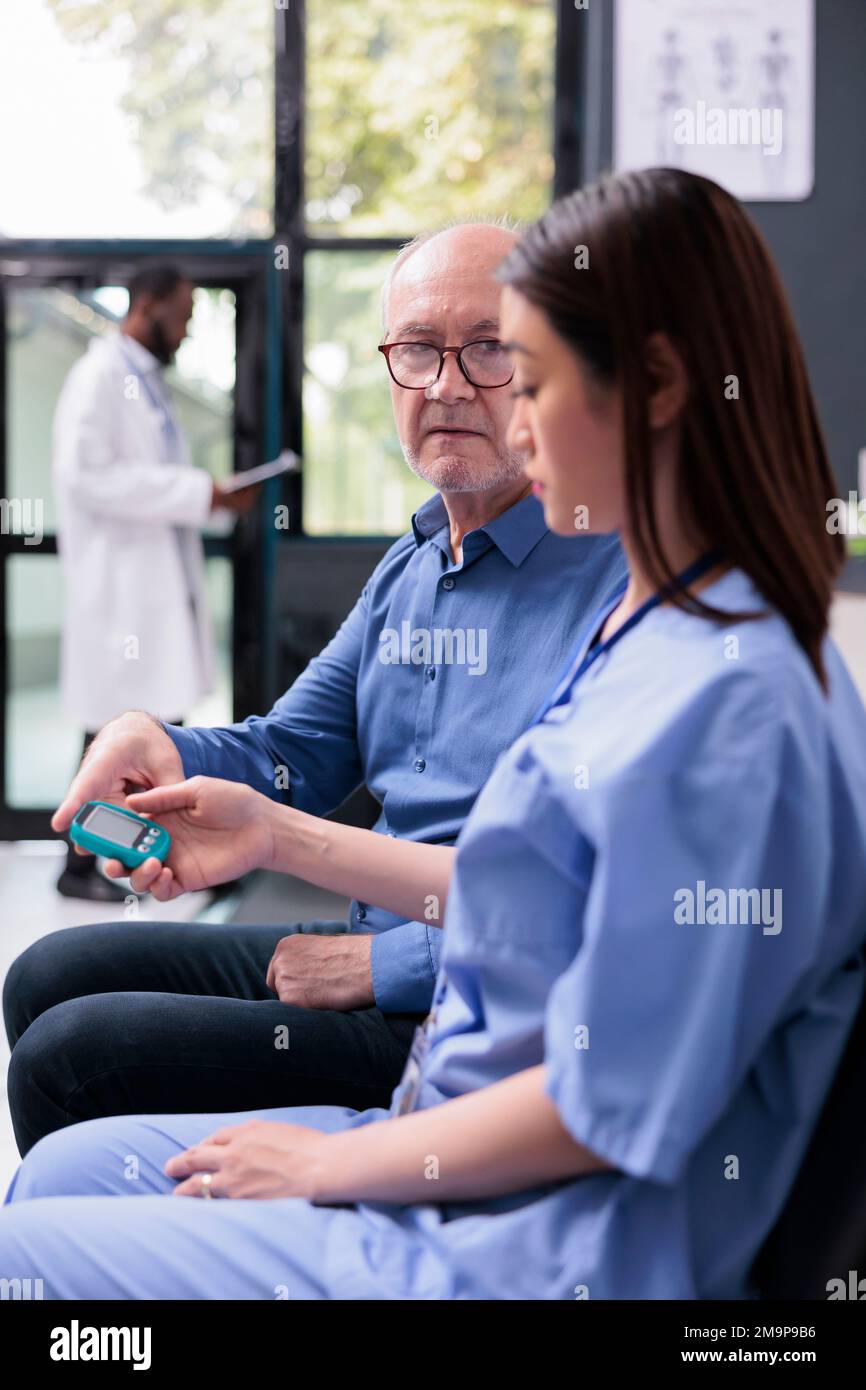 Asian medical asssistant consulting senior patient with glucometer ...