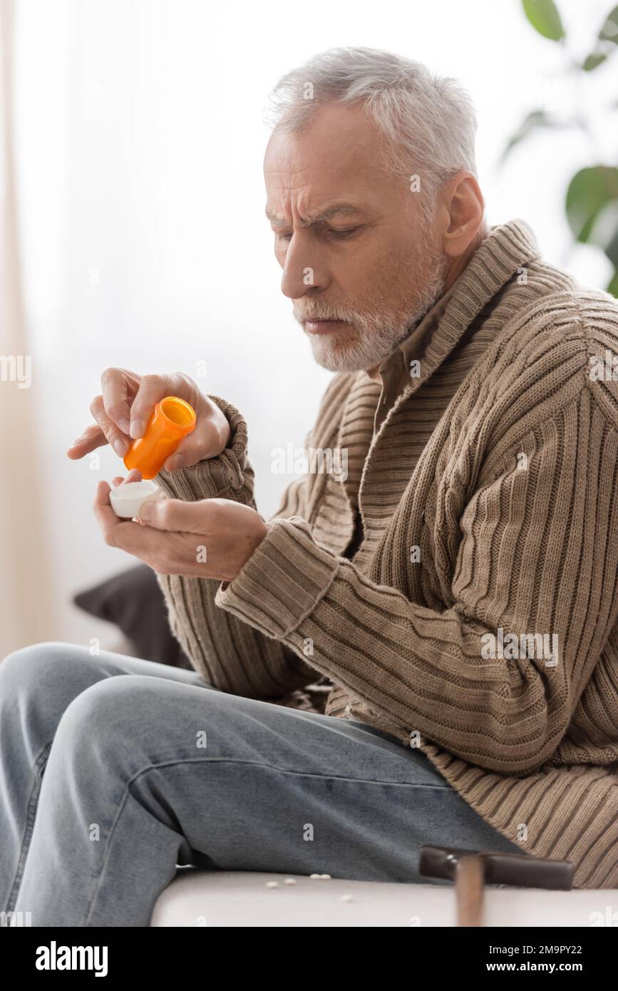 senior man in knitted cardigan holding pills container in trembling ...