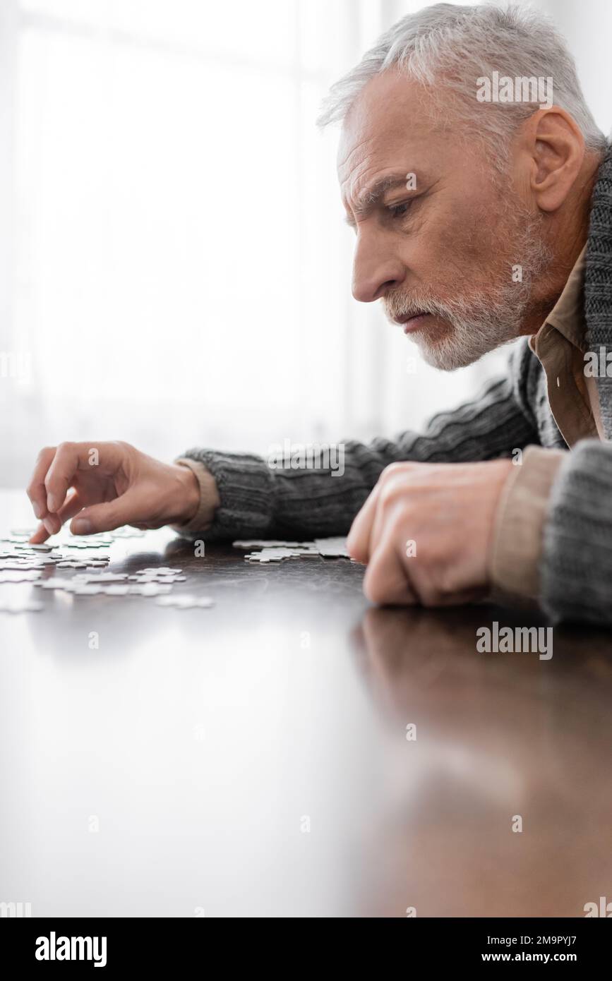 side view of aged man with parkinson syndrome combining jigsaw puzzle ...