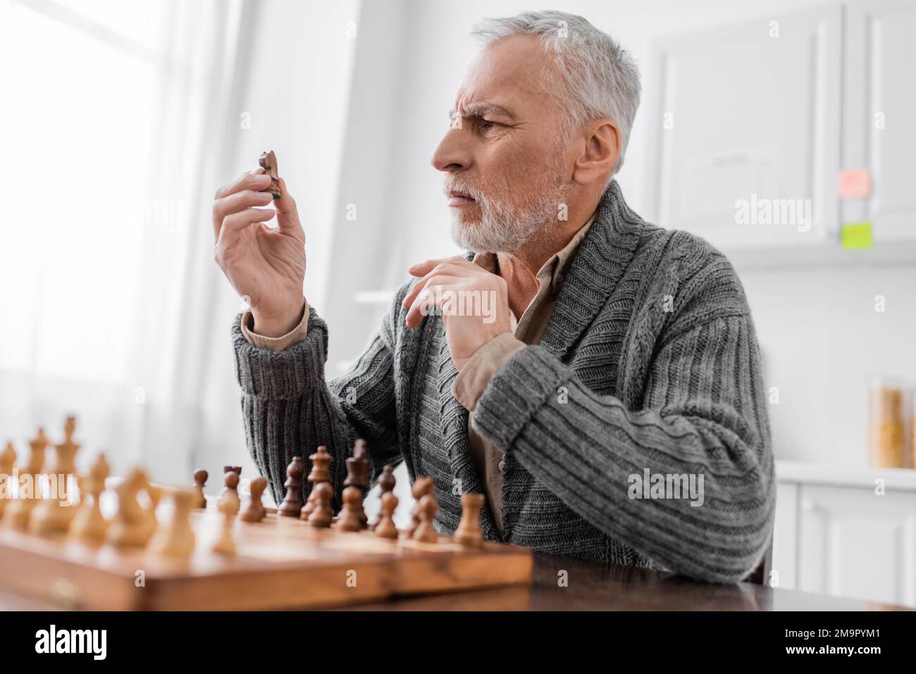 tense man suffering from memory loss and looking at chess figure while ...