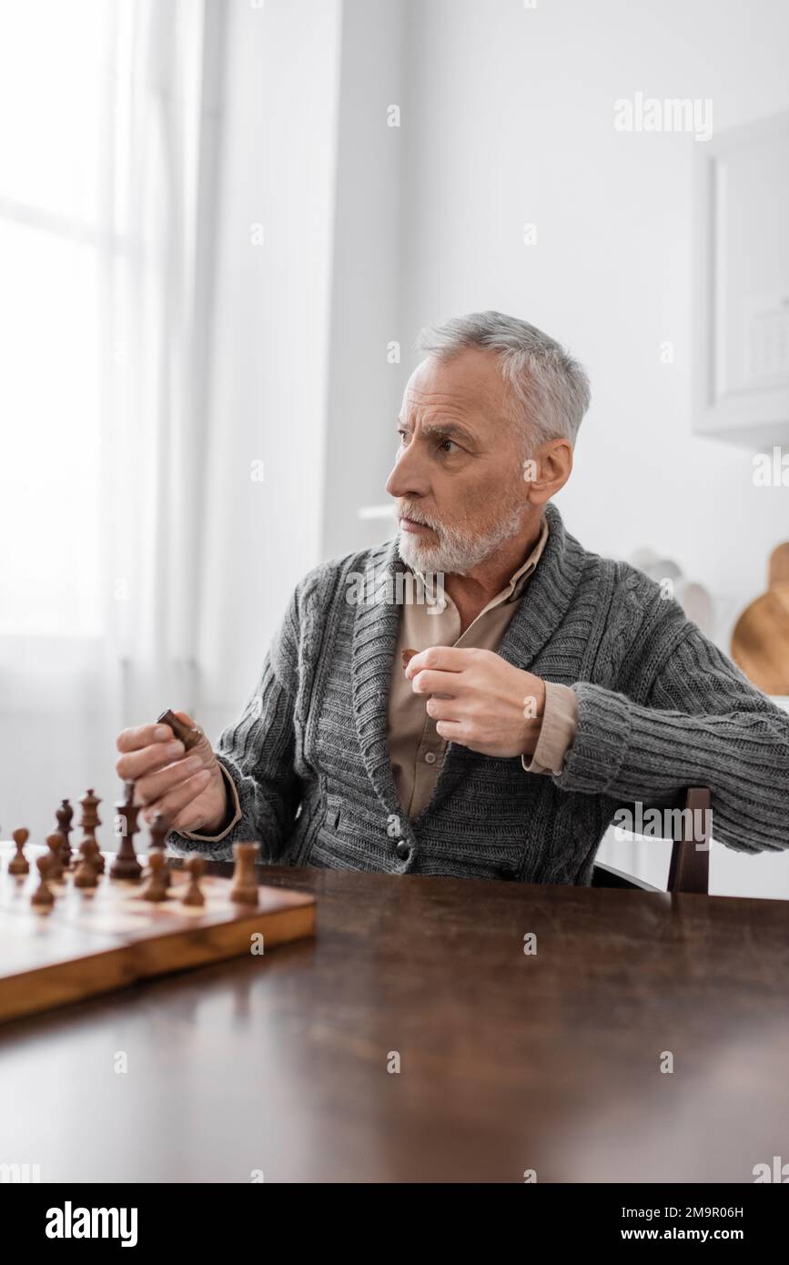 aged man with alzheimer disease holding chess figure and looking away ...