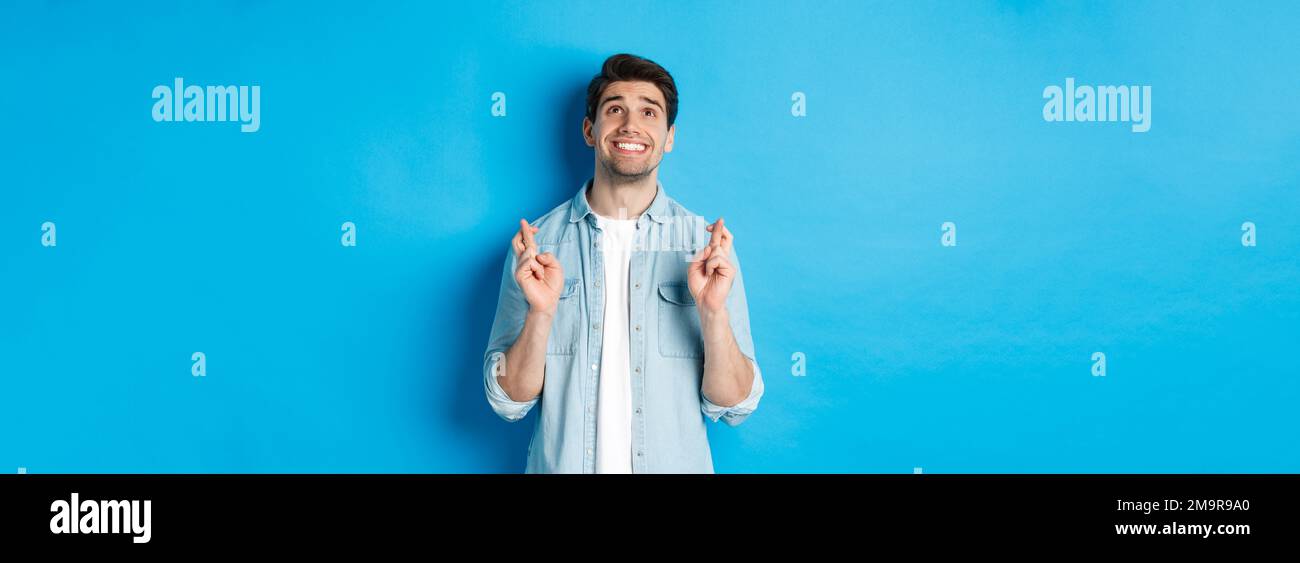 Lucky guy praying and making wish with crossed fingers, looking up with ...