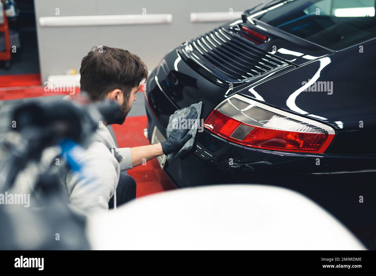 Man polishing spoiler of a black sports car with a cloth. Car detailing ...