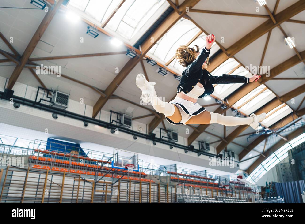 Side view of a cheerleader in the sports hall doing a split in the air ...