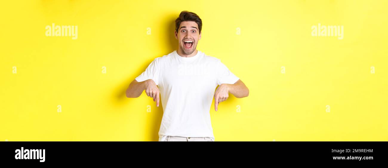 Amazed handsome man pointing fingers down, showing banner with ...