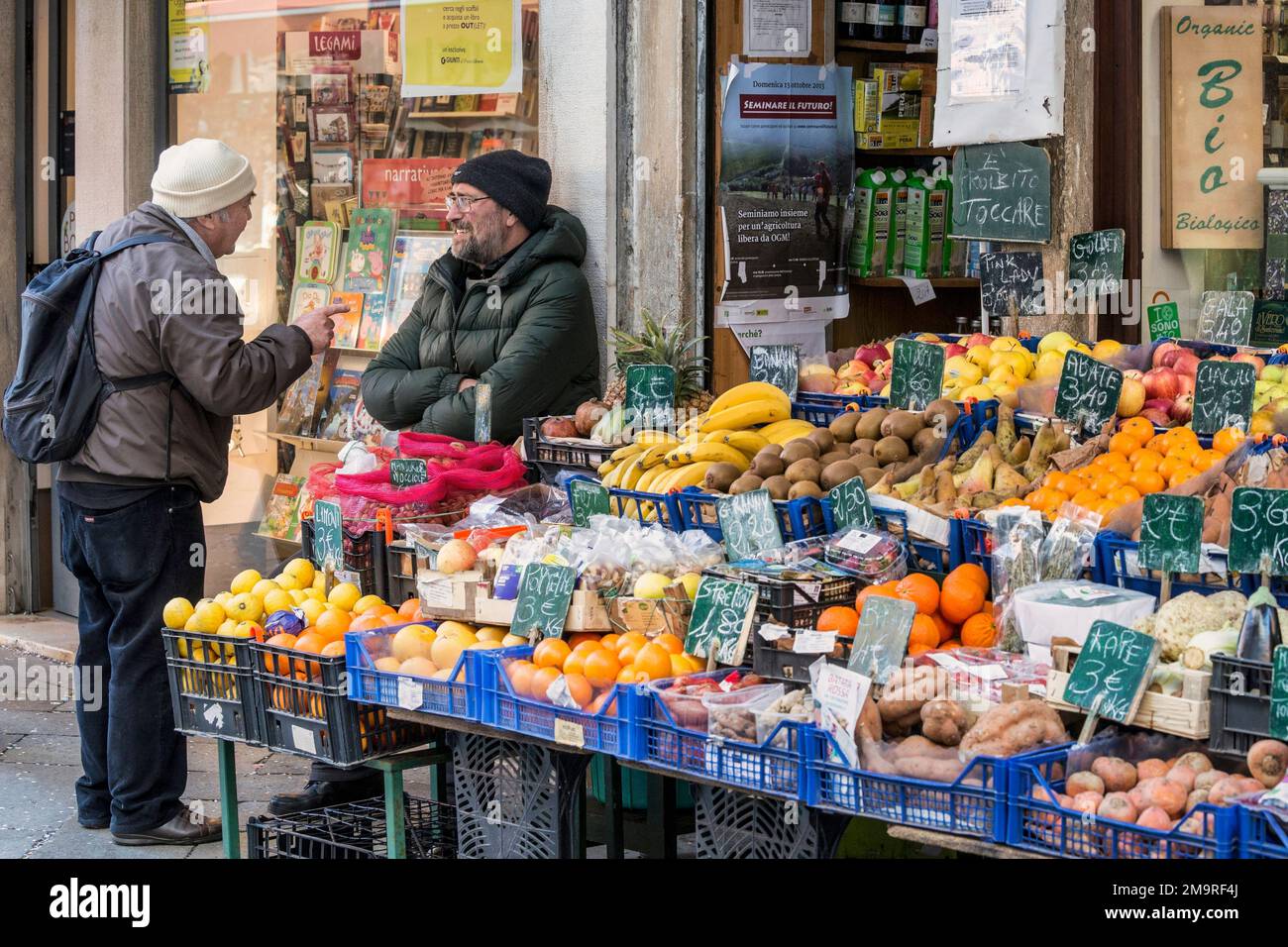 A shopkeeper talks to a customer by his display of fresh produce on a ...