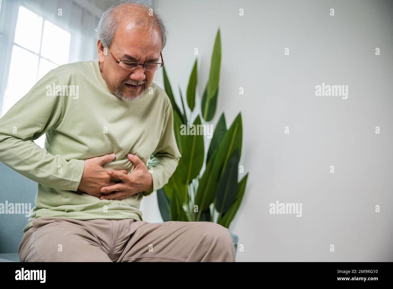 Senior Asian man sitting on sofa having suffering from stomach ache ...