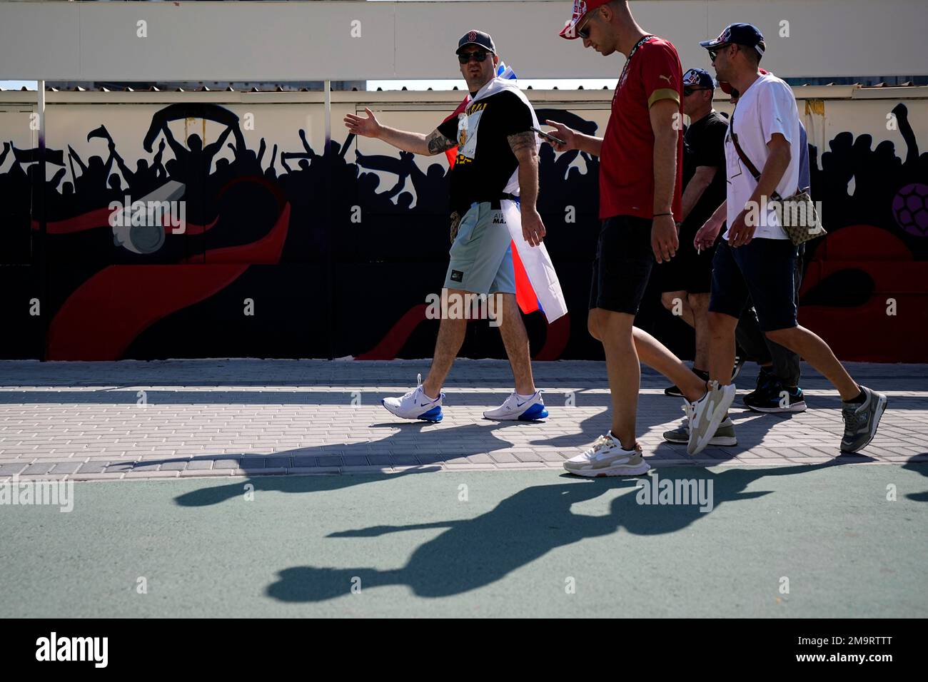 Soccer fans walk on a street along the wall painting for Qatar 2022 ...