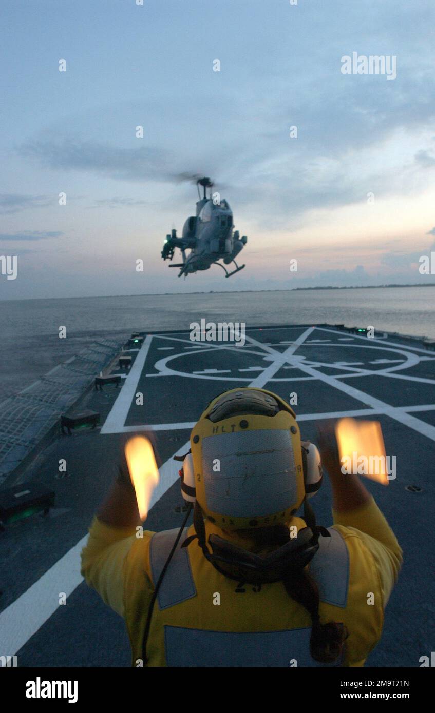 US Navy (USN) Sailor Lou Robinson, uses light wands to guide an AH-1W ...