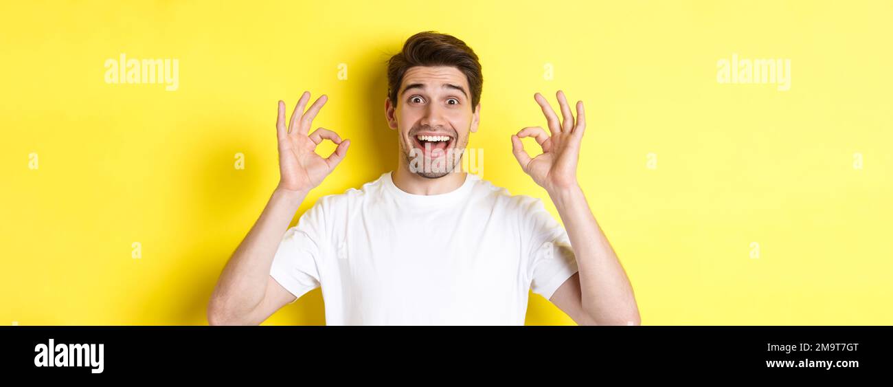 Amazed young man showing ok signs and smiling, recommending something ...