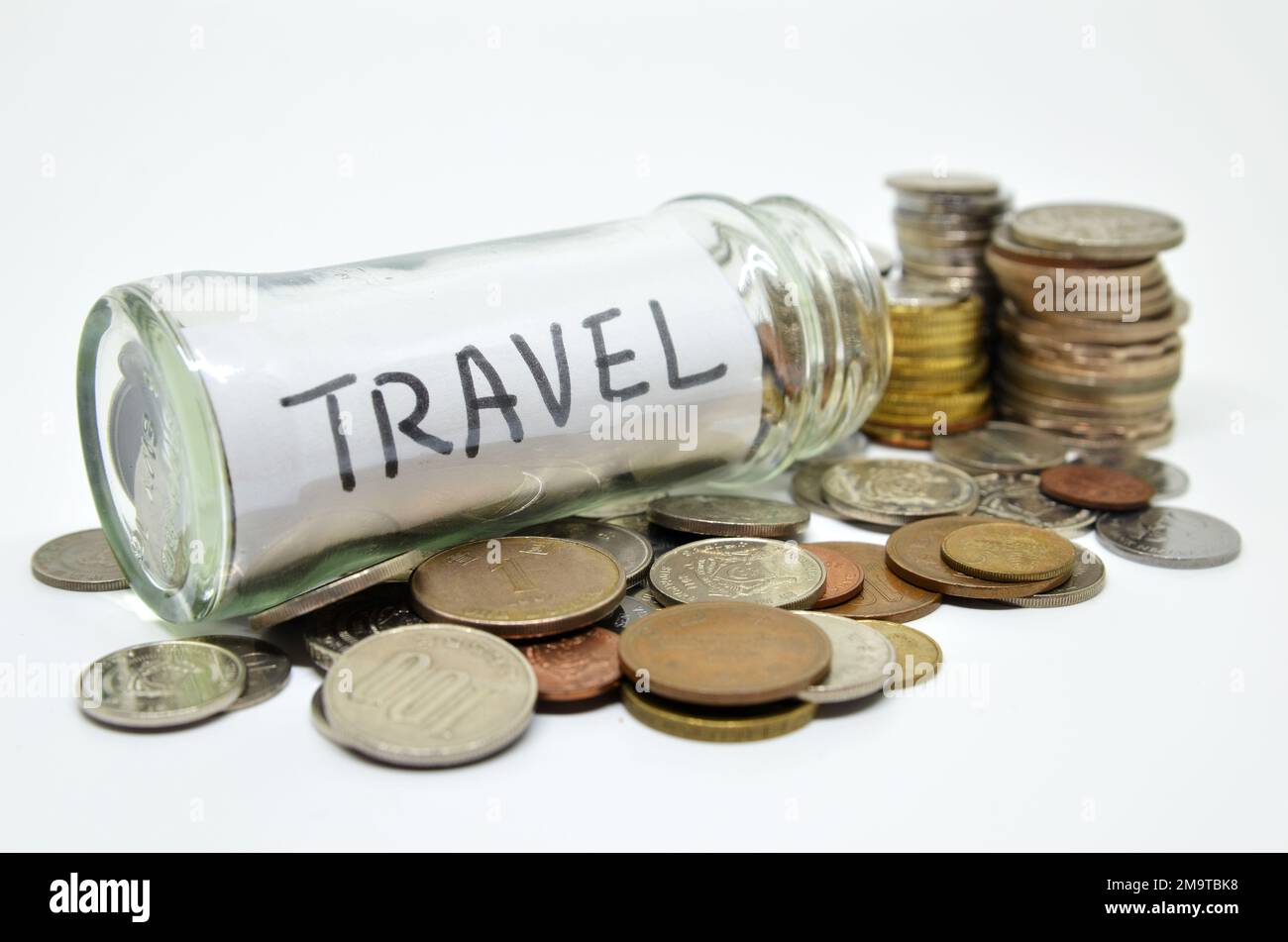 Travel lable in a glass jar with coins spilling out isolated on white ...