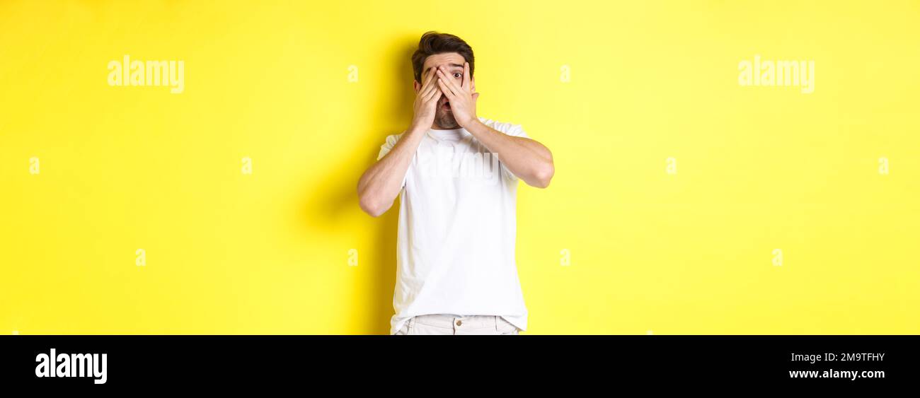 Embarrassed guy shut eyes but peeking through fingers at something ...