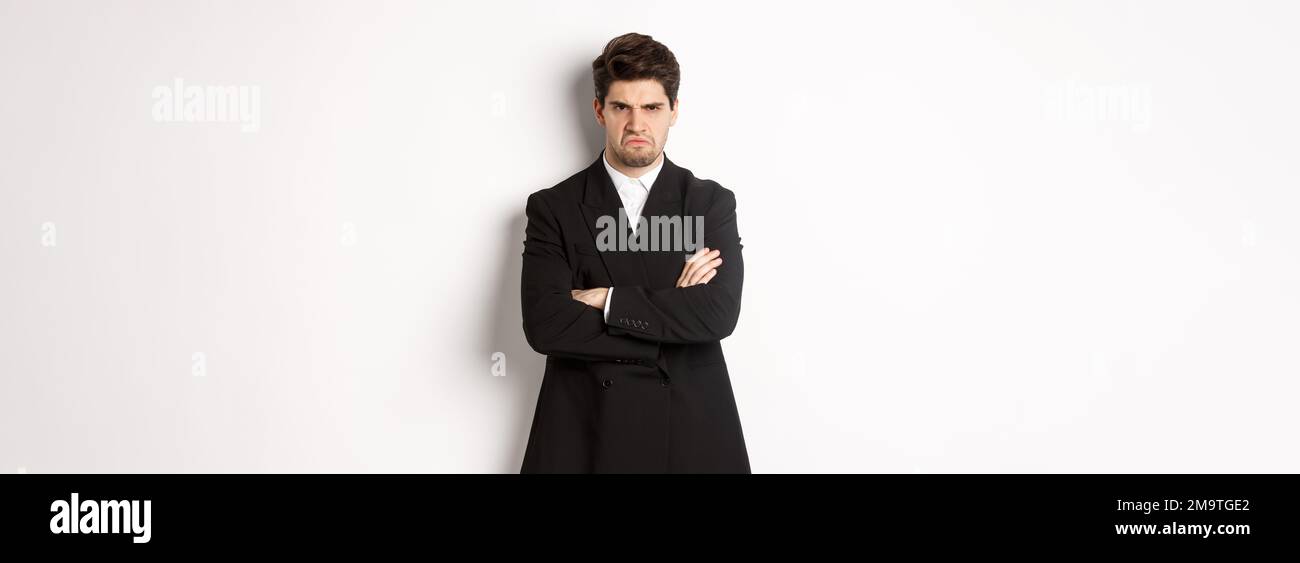 Portrait of angry handsome man in black suit, cross arms on chest and ...