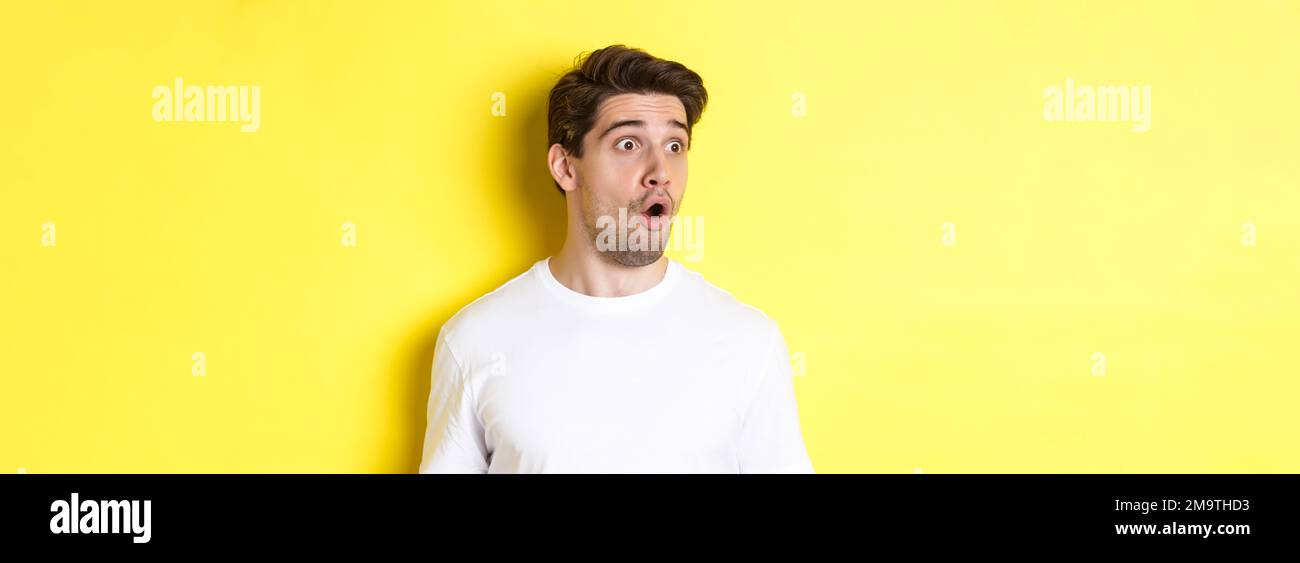 Close-up of impressed man looking left, gasping amazed, standing in ...