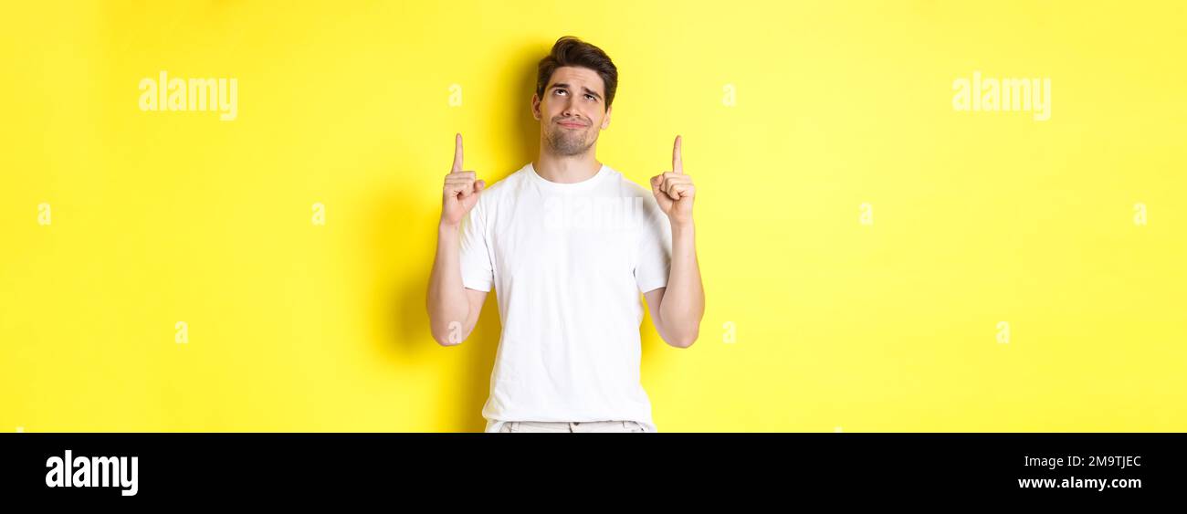 Skeptical young man pointing and looking up at something bad, judging ...