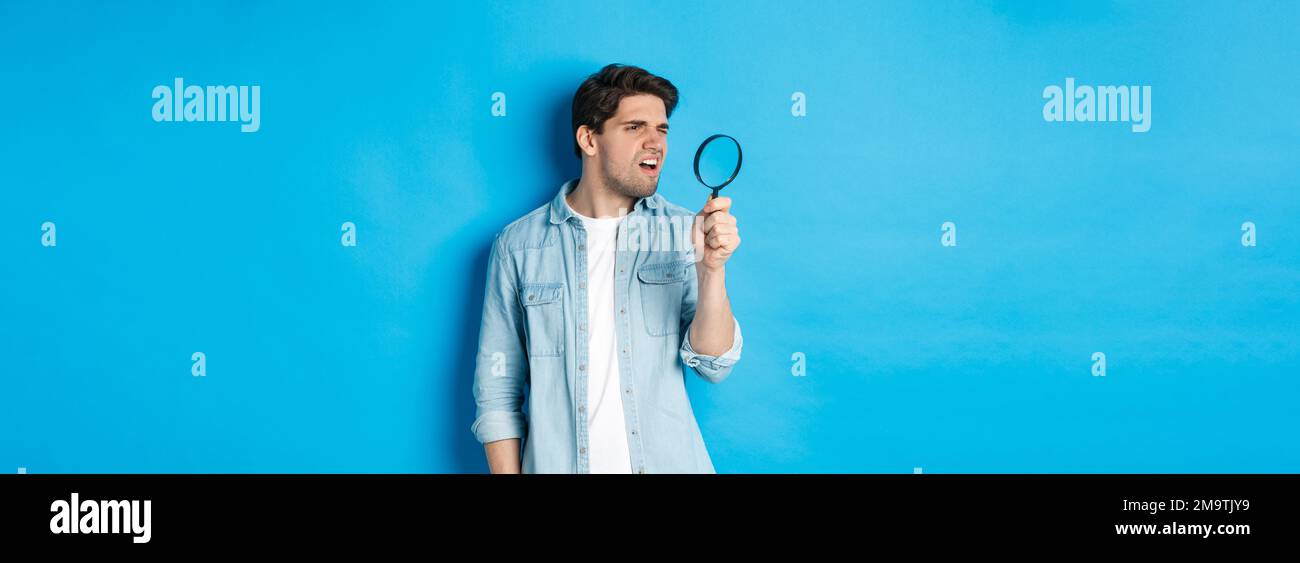 Young thoughtful guy looking through magnifying glass, reading ...