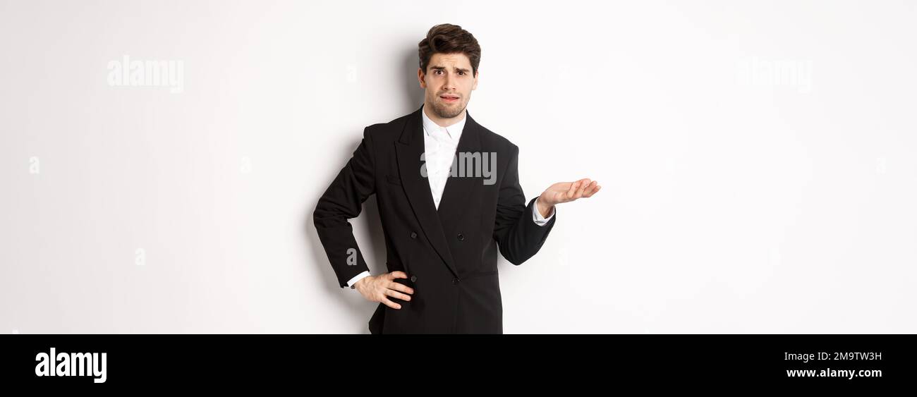Image of confused handsome man in formal suit, raising hand and ...