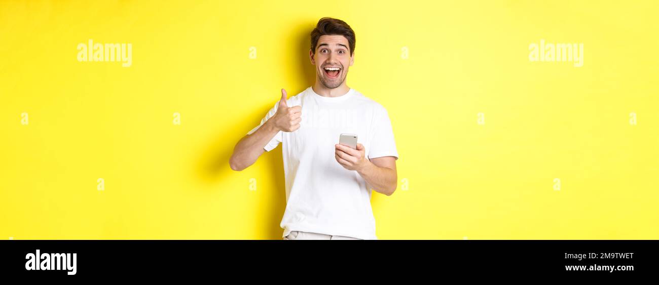 Happy smiling man holding smartphone, showing thumb up in approval ...