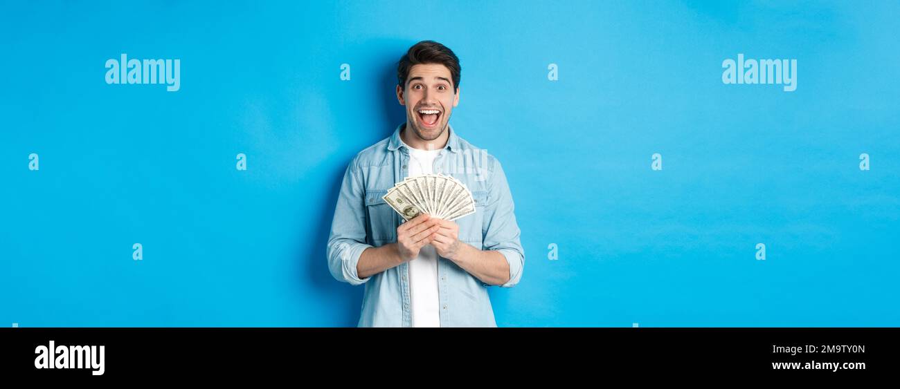 Excited and surprised attractive man, holding money prize and smiling ...