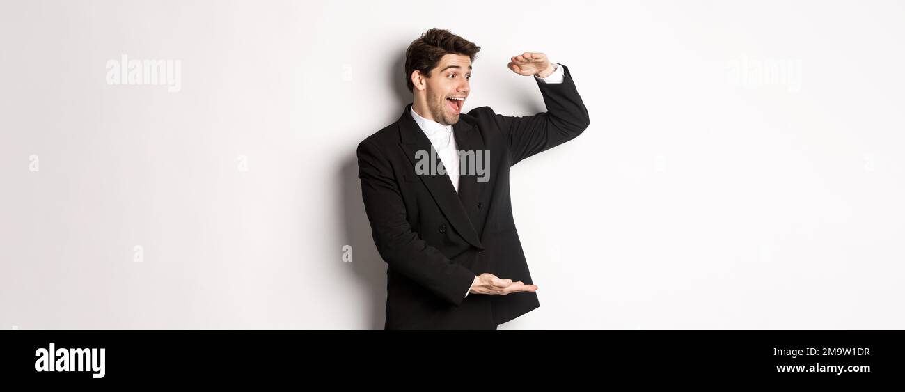 Portrait of excited handsome man in suit, shaping big object on copy ...