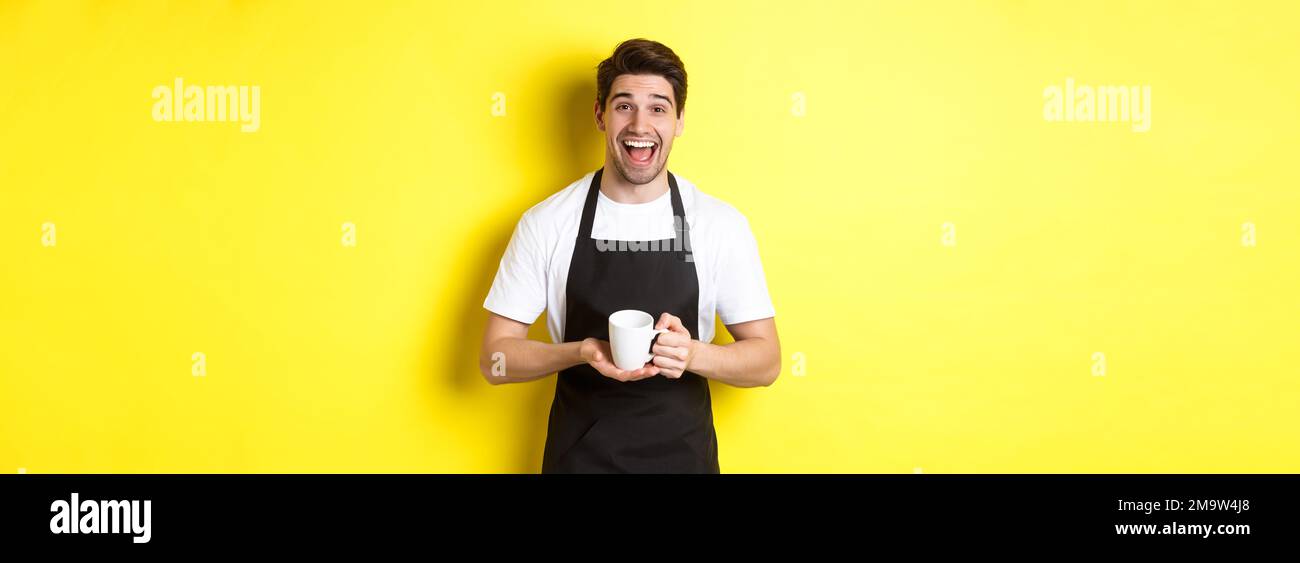 Happy barista in black apron holding coffee cup, laughing and standing ...
